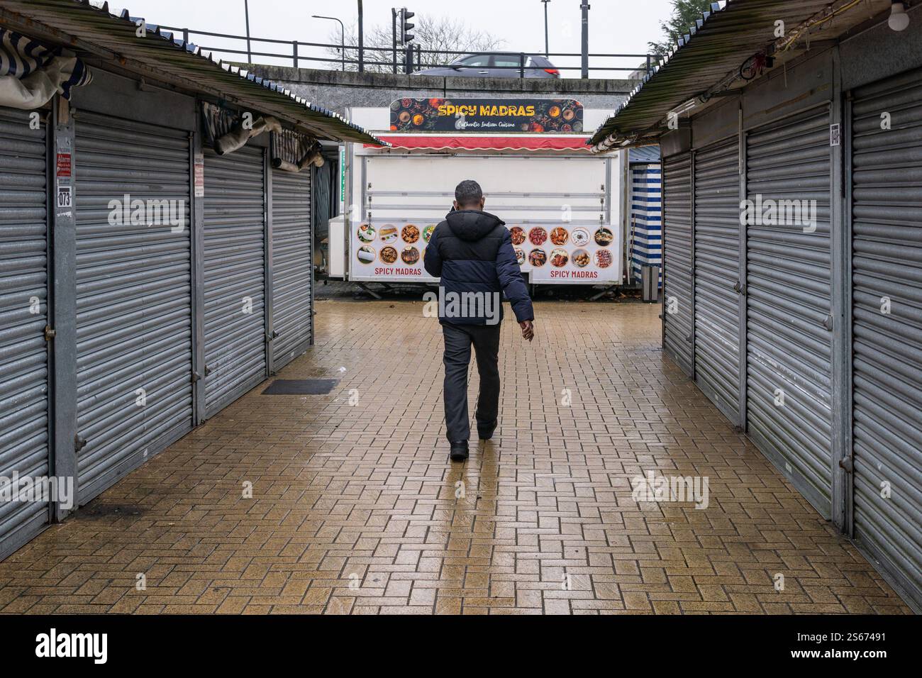 Rear view of a man walking through a closed and shuttered market stalls ...