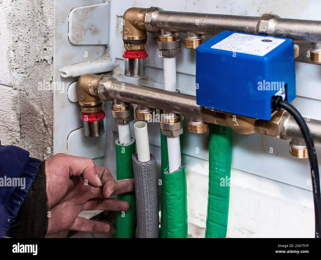 Close-up of a plumbing system with green insulation and a blue control ...