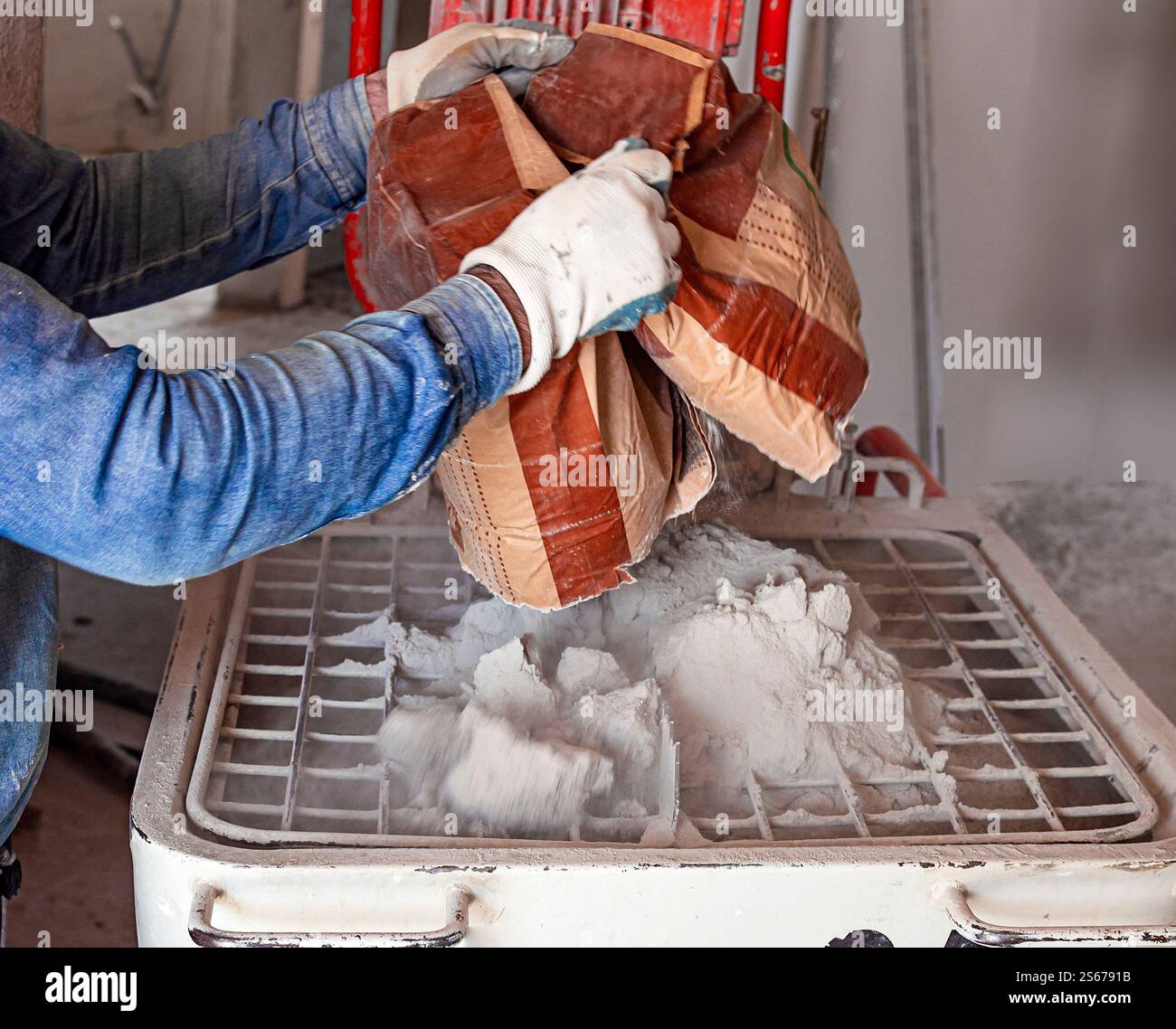 worker pours a bag of dry plaster into the hopper for mixing dry ...