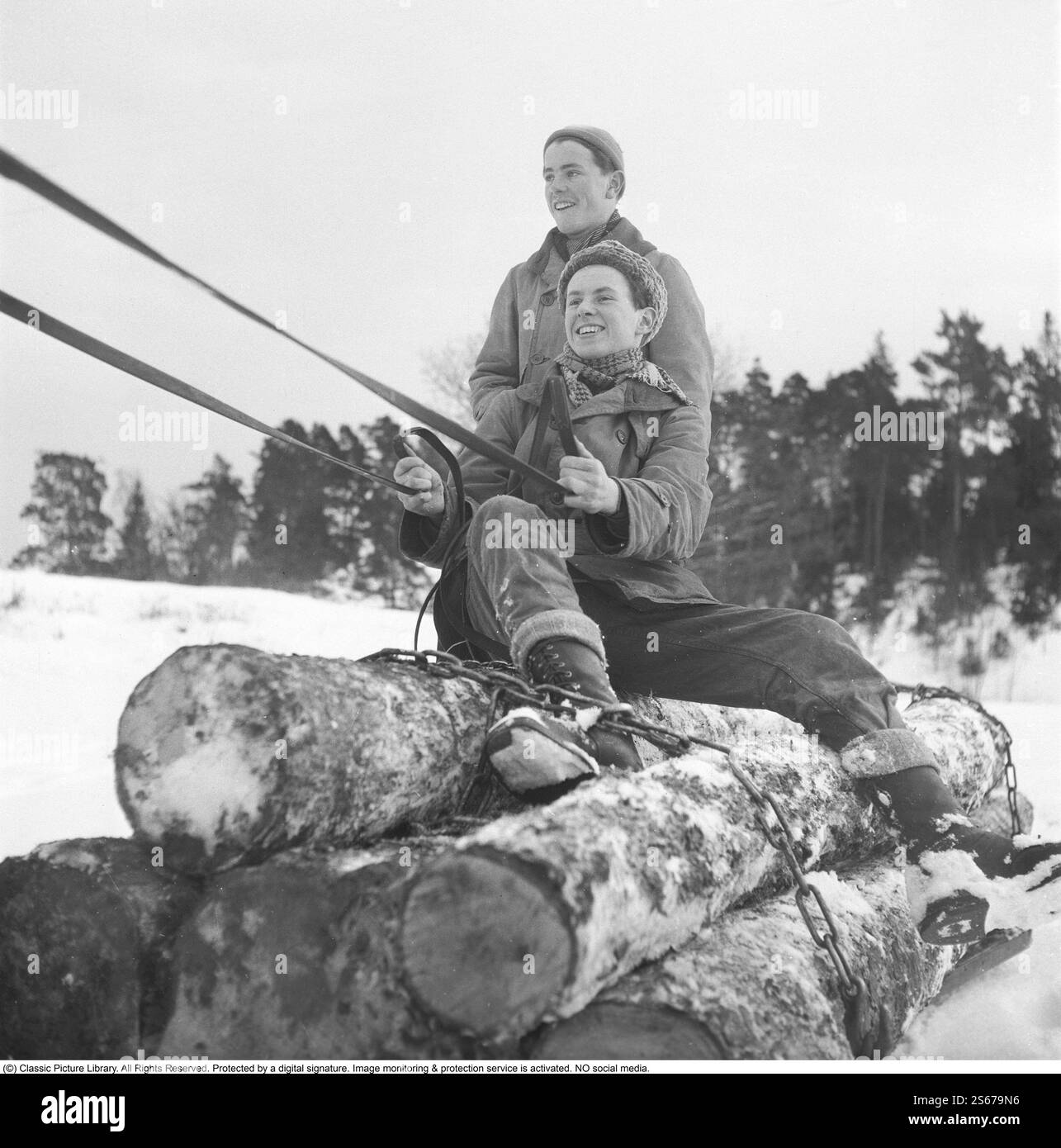 In the 1950s. Two men are sitting on a sleigh with wooden logs with a ...