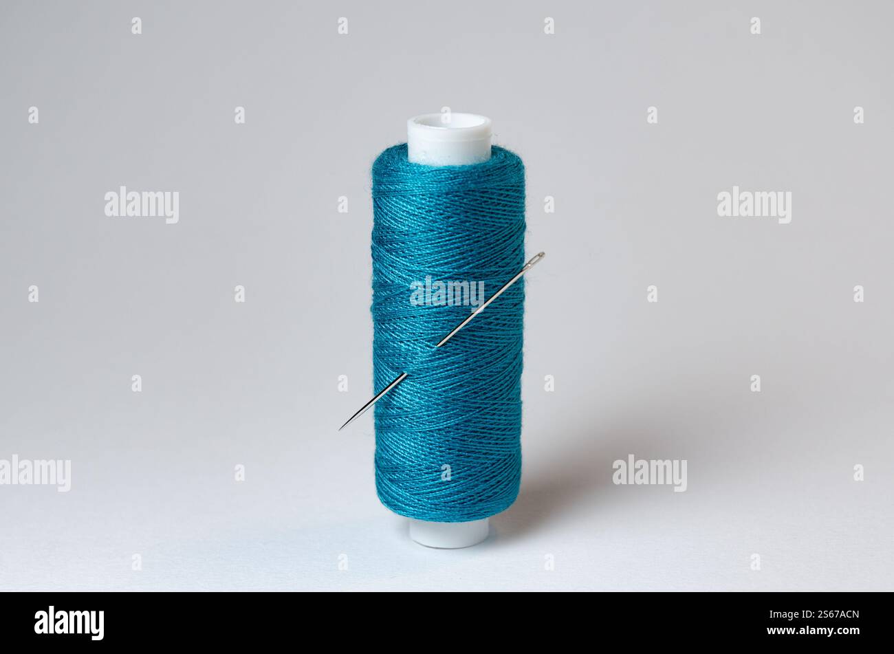 One single turquoise thread spool with needle on white background Stock ...