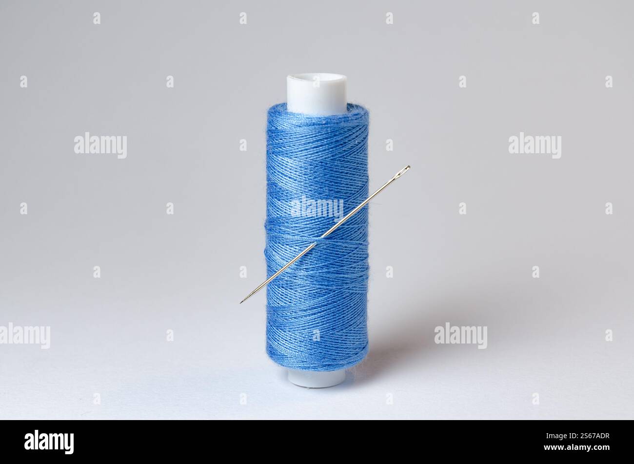 One single light blue thread spool with needle on white background ...