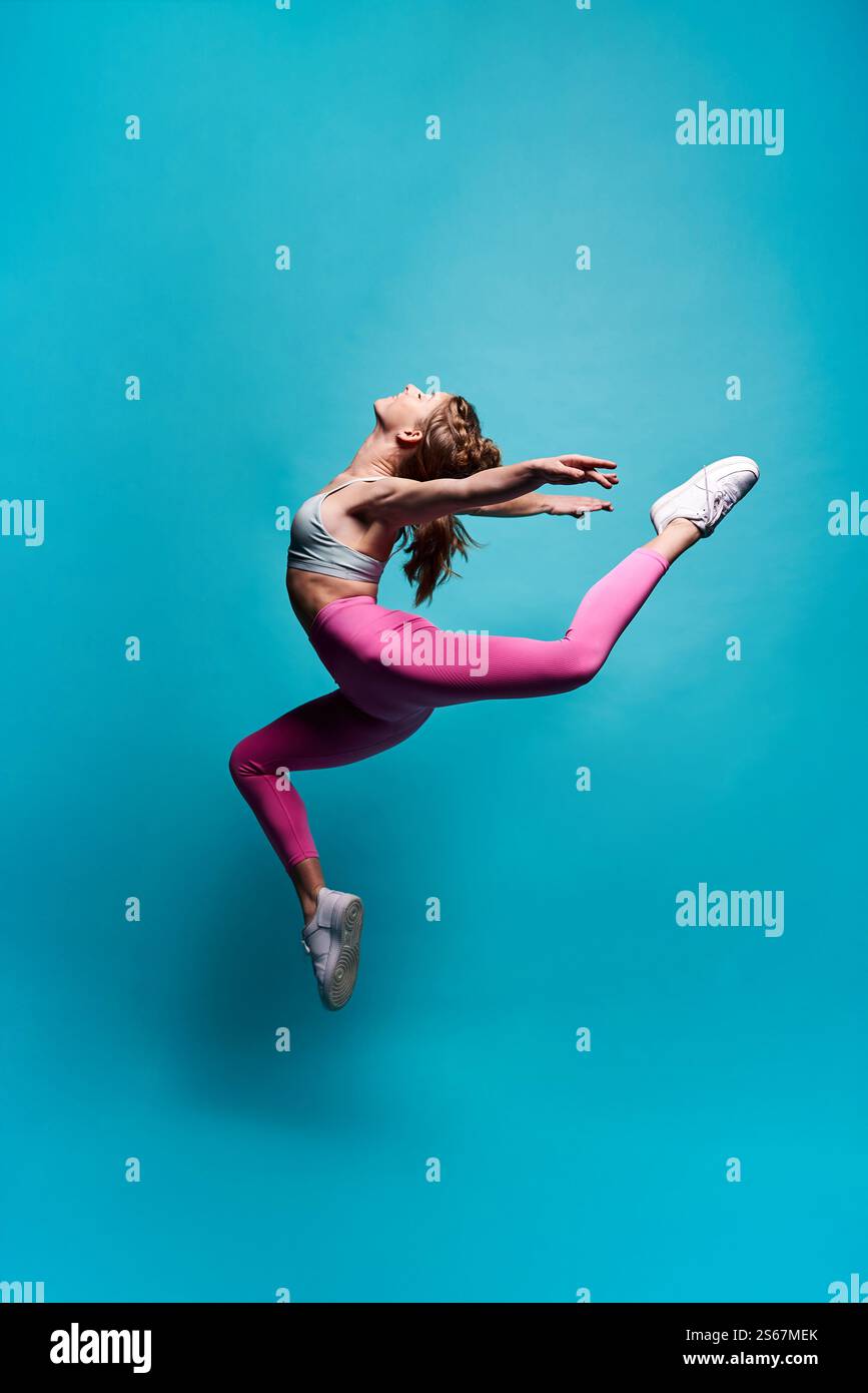 Flexible dancer in mid-air leap wearing sporty attire on a vivid blue ...
