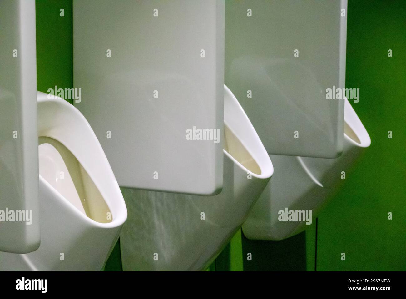 Three white urinals attached to a bright green wall Stock Photo - Alamy