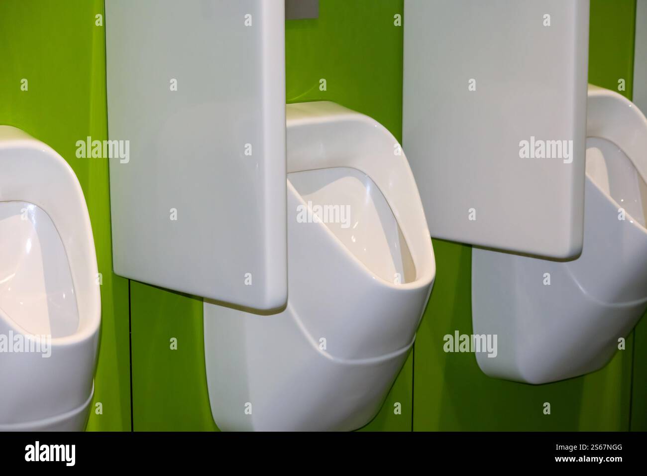 Three white urinals attached to a bright green wall Stock Photo - Alamy