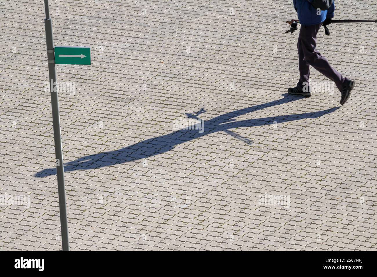 A man with sticks in his hands walking along a paved path following a ...
