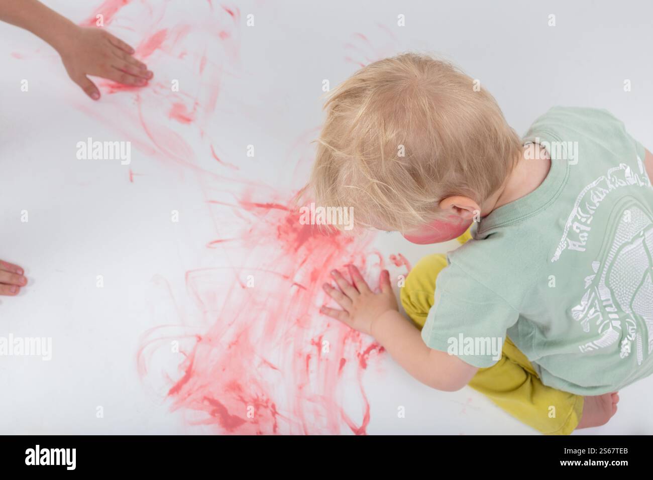 Baby joyfully finger painting with vibrant red color on a large sheet ...