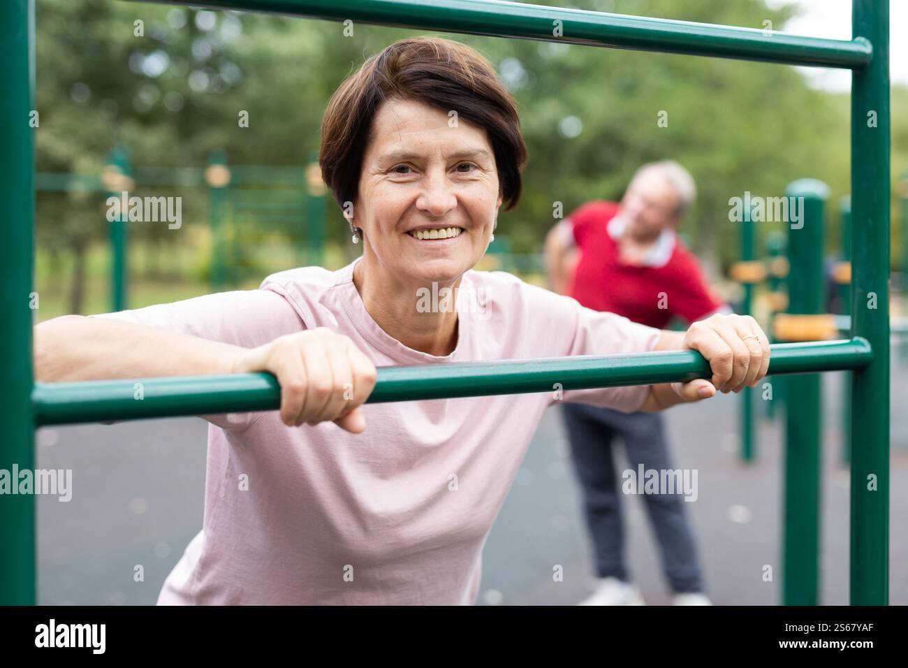 Mature woman doing push-ups from the crossbar on outdoor sports ground ...