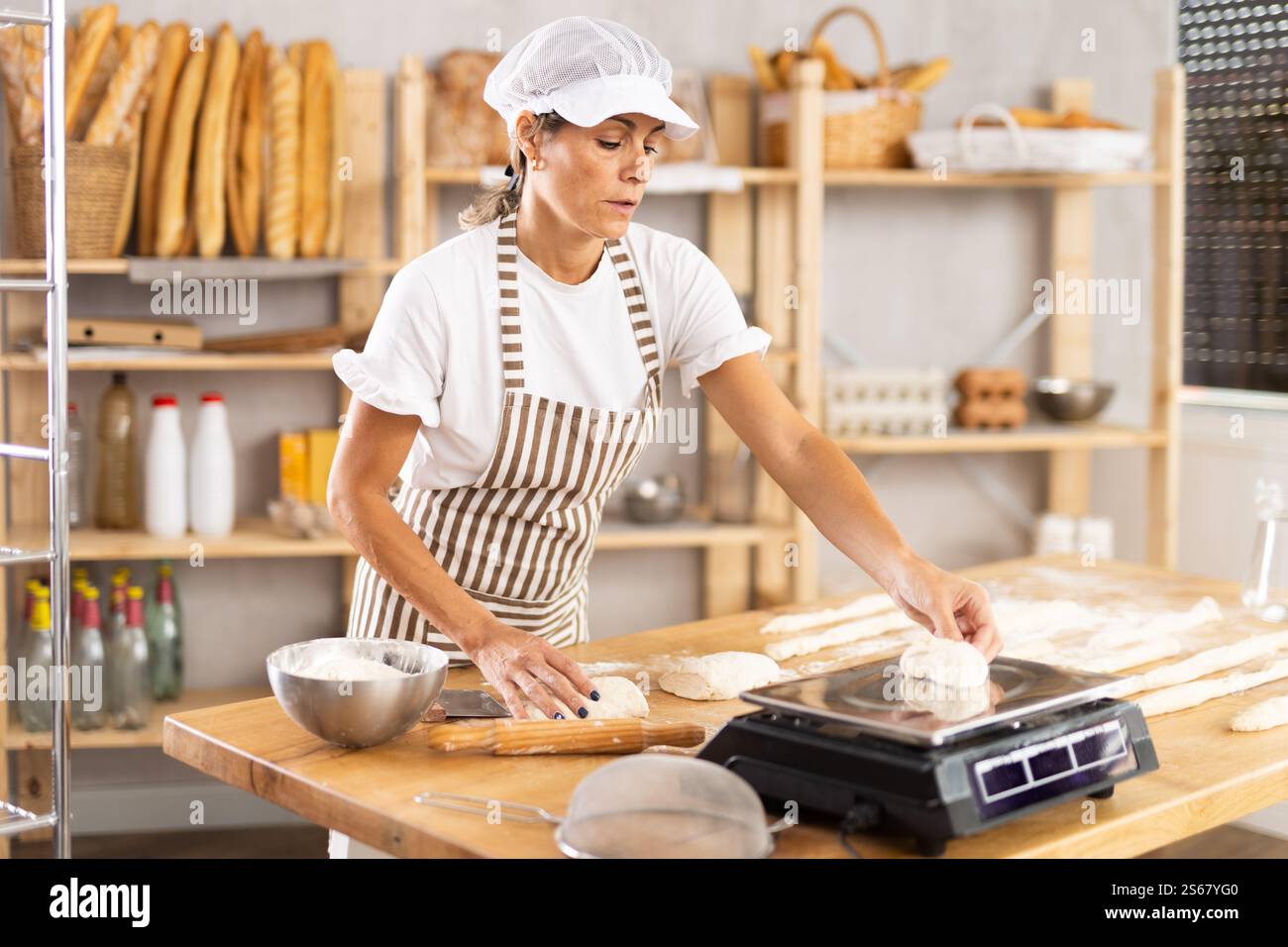 Female baker prepares raw dough, cuts pieces and weighs them on scale ...