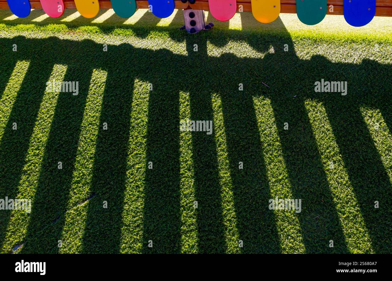 A colorful playground fence casting long striped shadows on artificial ...