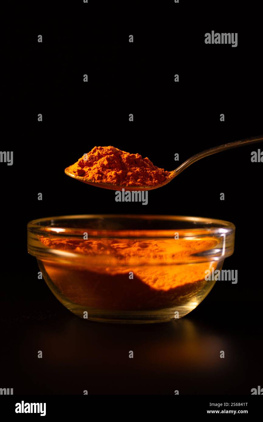 Spoon of turmeric powder isolated on dark background. Vibrant orange ...