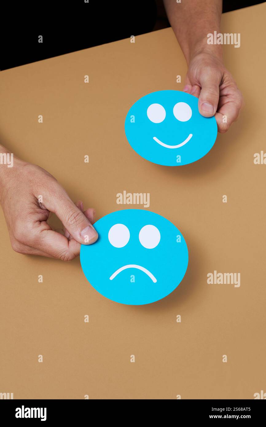 closeup of a man holding a blue paper sad face and a blue paper happy ...