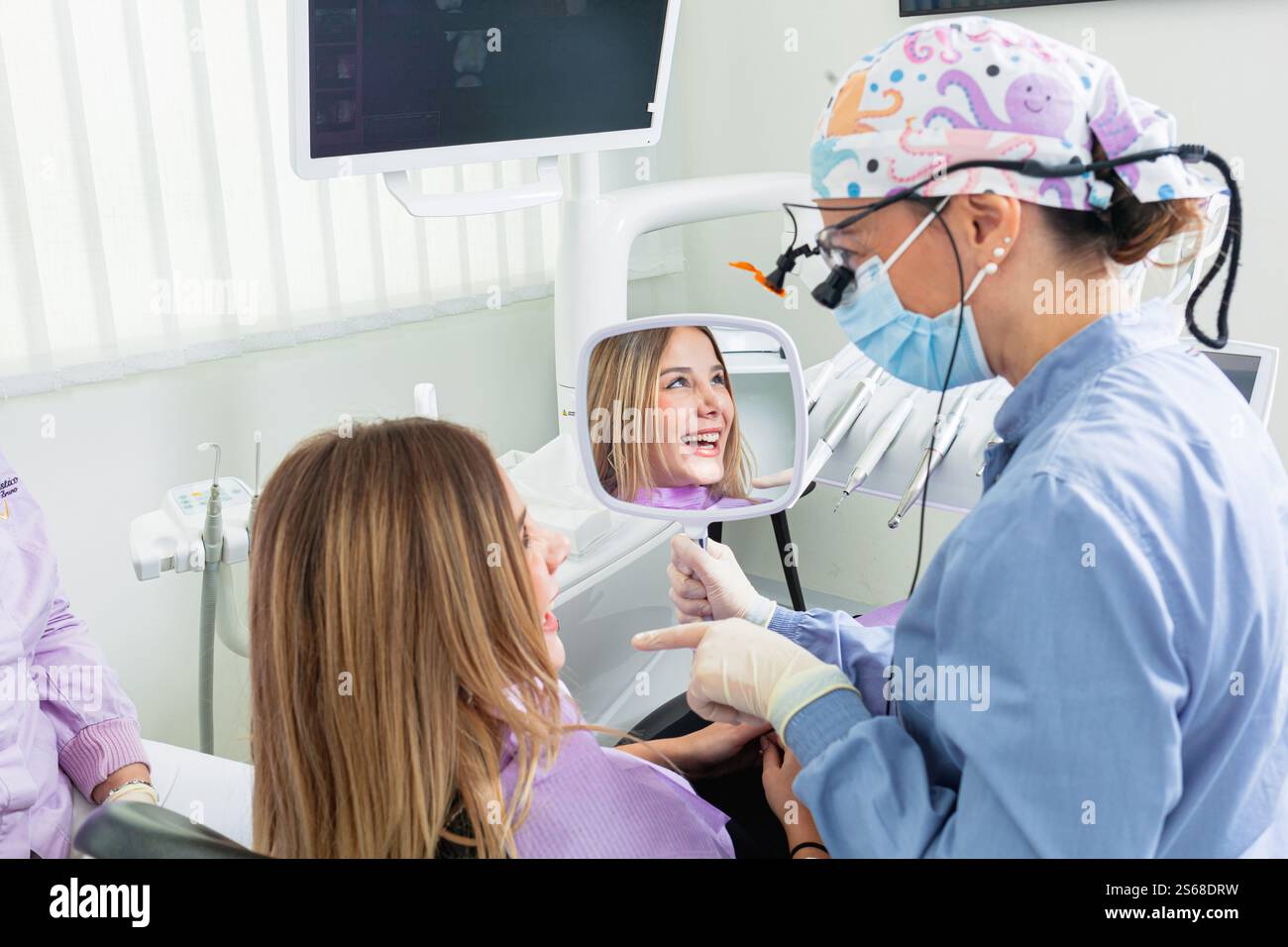 Female dentist pointing at mirror, showing treatment result to satisfied patient in dental ...