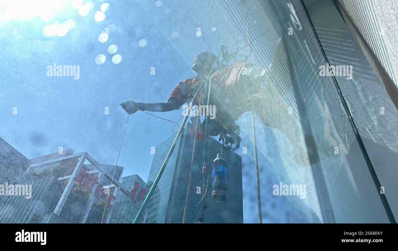 Window cleaner in a safety harness hanging on a rope outside a high ...