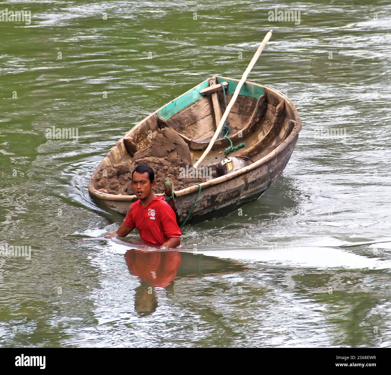 A man collecting river sand into his small boat from a river bed in ...