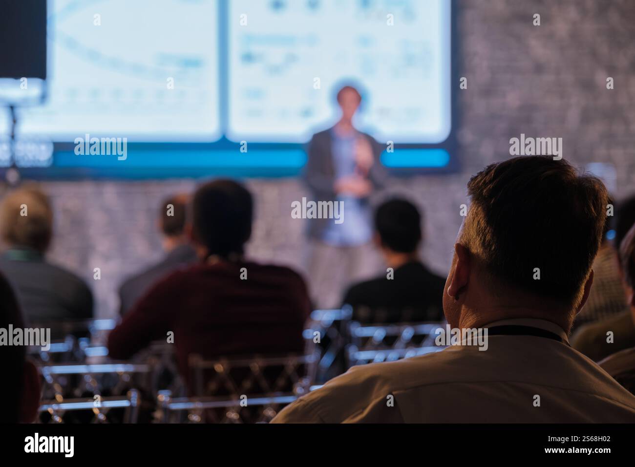 Group of people attentively watching presentation with speaker visible ...