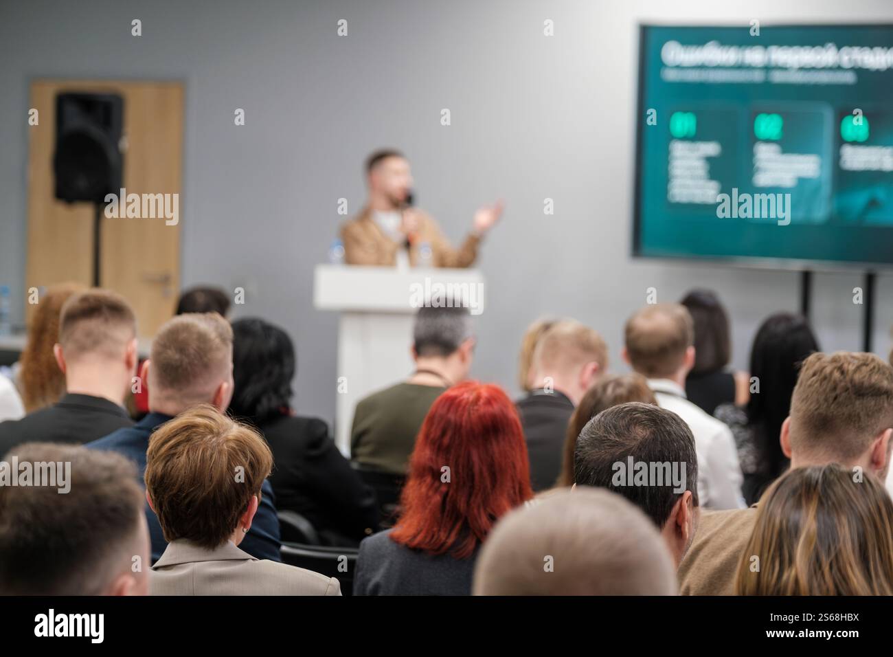 Speaker delivers presentation to attentive audience at business event. Large screen displays ...