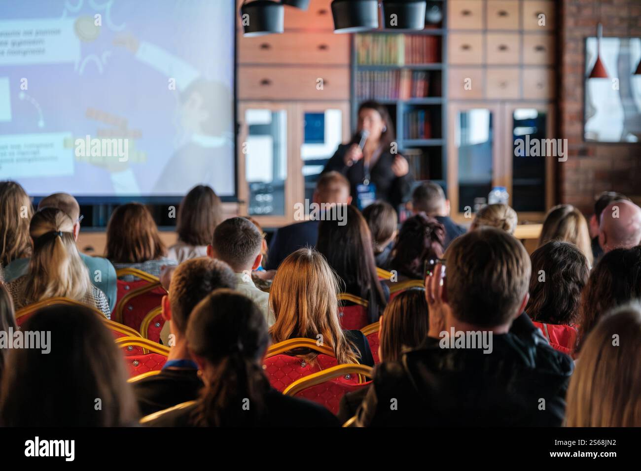 Audience seated in a modern conference venue listening to a speaker ...
