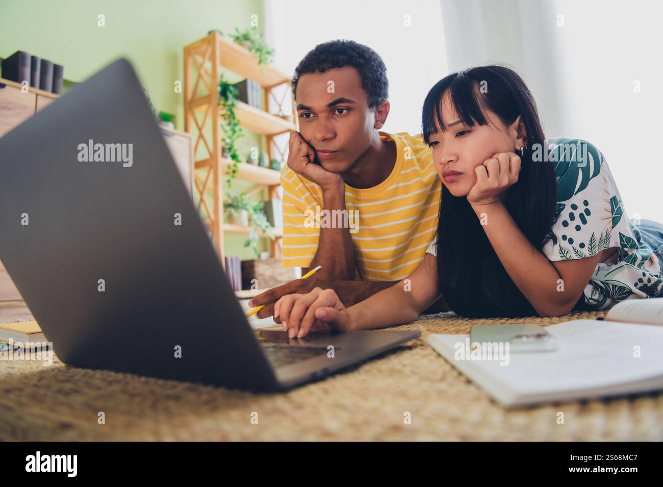 Photo of charming lovely clever couple lying floor doing homework ...