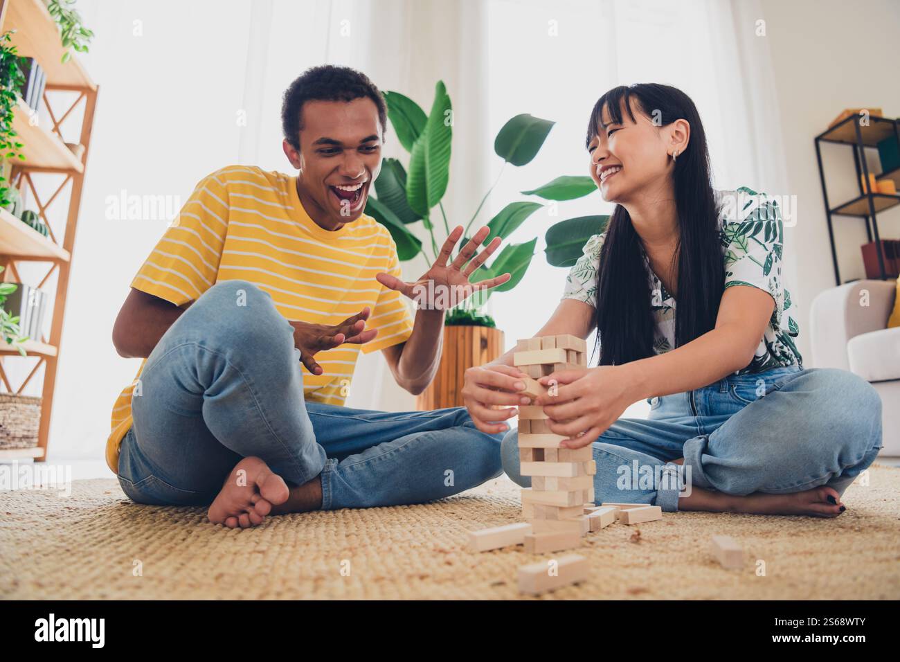Photo of beautiful cheerful multinational couple sit floor play jenga ...