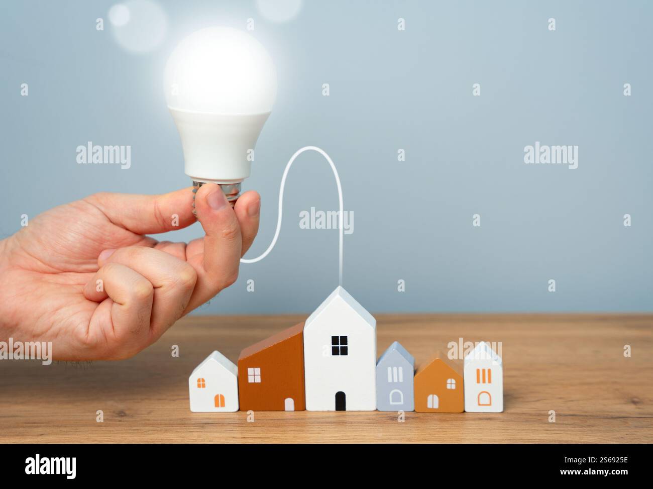 Hand connects light bulb to residential buildings. Concept of power ...