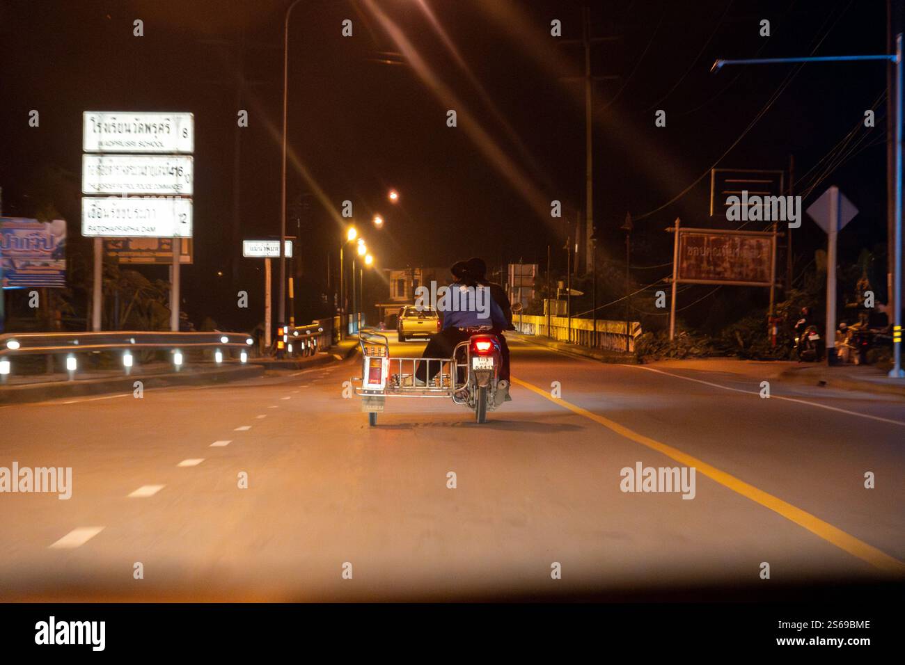 Motorcycle with sidecar drives along a quiet road at night in a rural ...