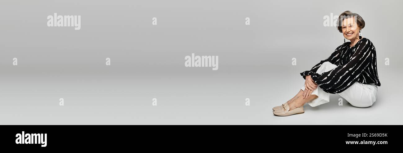 A stylish woman in her 60s poses gracefully in elegant attire against a ...