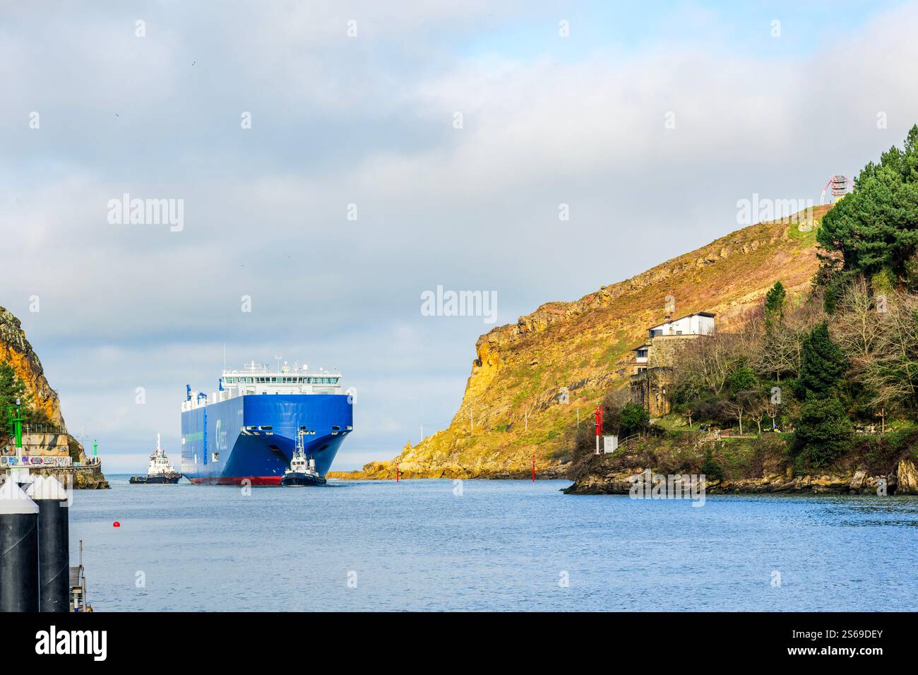A large hybrid-powered cargo ship docked in a harbor, accompanied by a ...