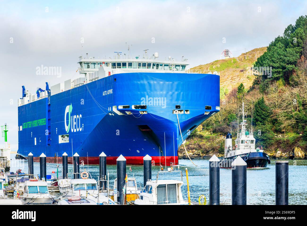 A large hybrid-powered cargo ship docked in a harbor, accompanied by a ...