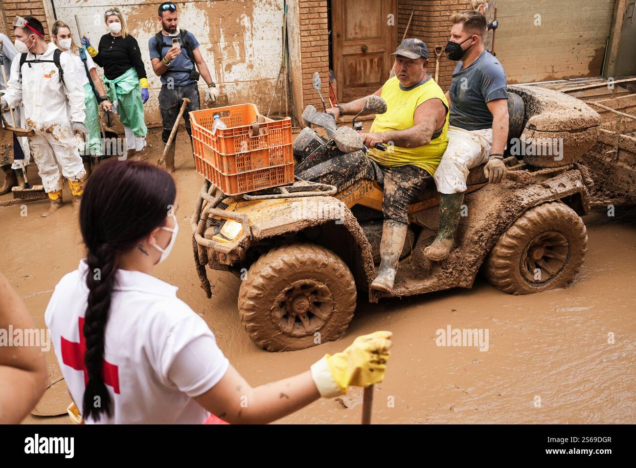 Two locals on a quad in a street covered in mud with volunteers and ...