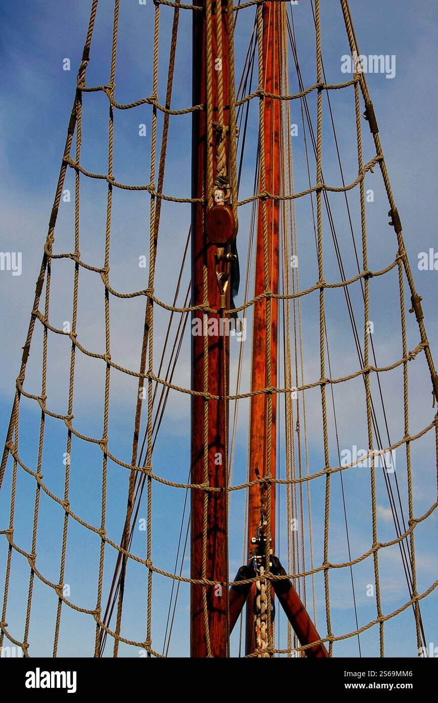 Wooden bowsprit, mast, safety netting and rigging, seen against the sky ...