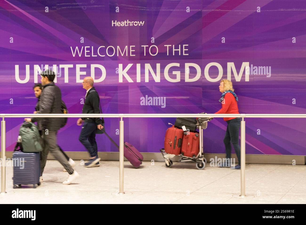 Travellers walk past the wall billboard "Welcome To The United Kingdom ...