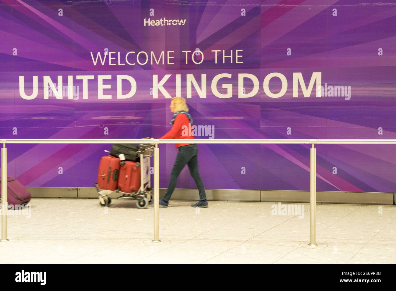 Travellers walk past the wall billboard "Welcome To The United Kingdom ...