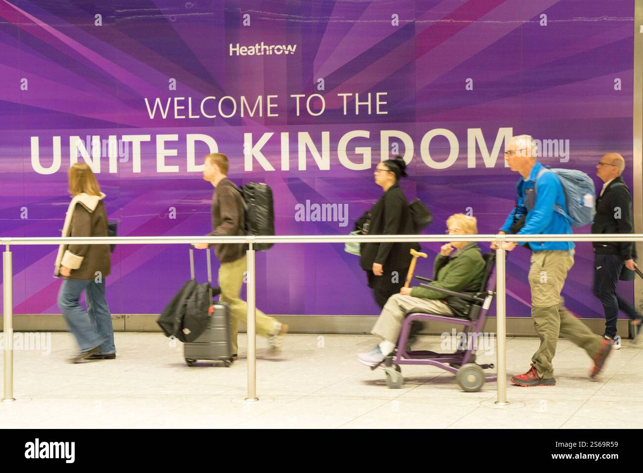 Travellers walk past the wall billboard "Welcome To The United Kingdom ...