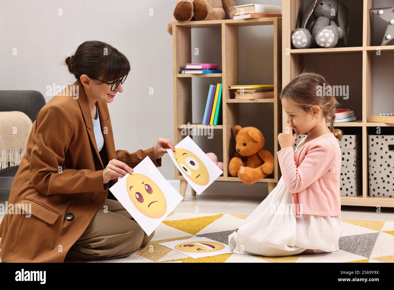 Autism therapy. Little girl choosing emoticon with smiling psychologist ...