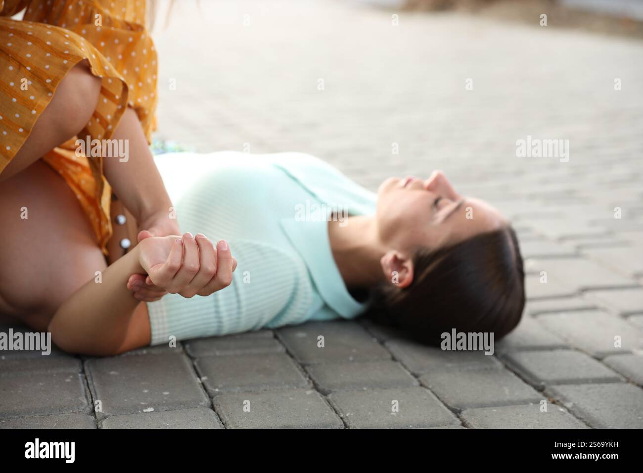 Woman checking pulse of unconscious person with heart attack on city ...