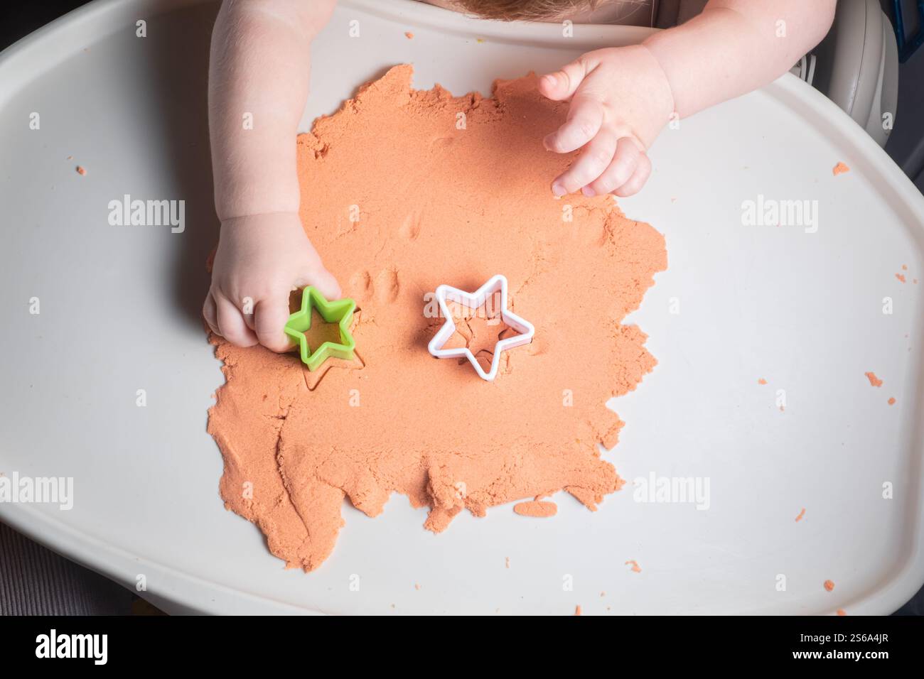faceless baby is playing with kinetic sand. Child handles with a toy in ...