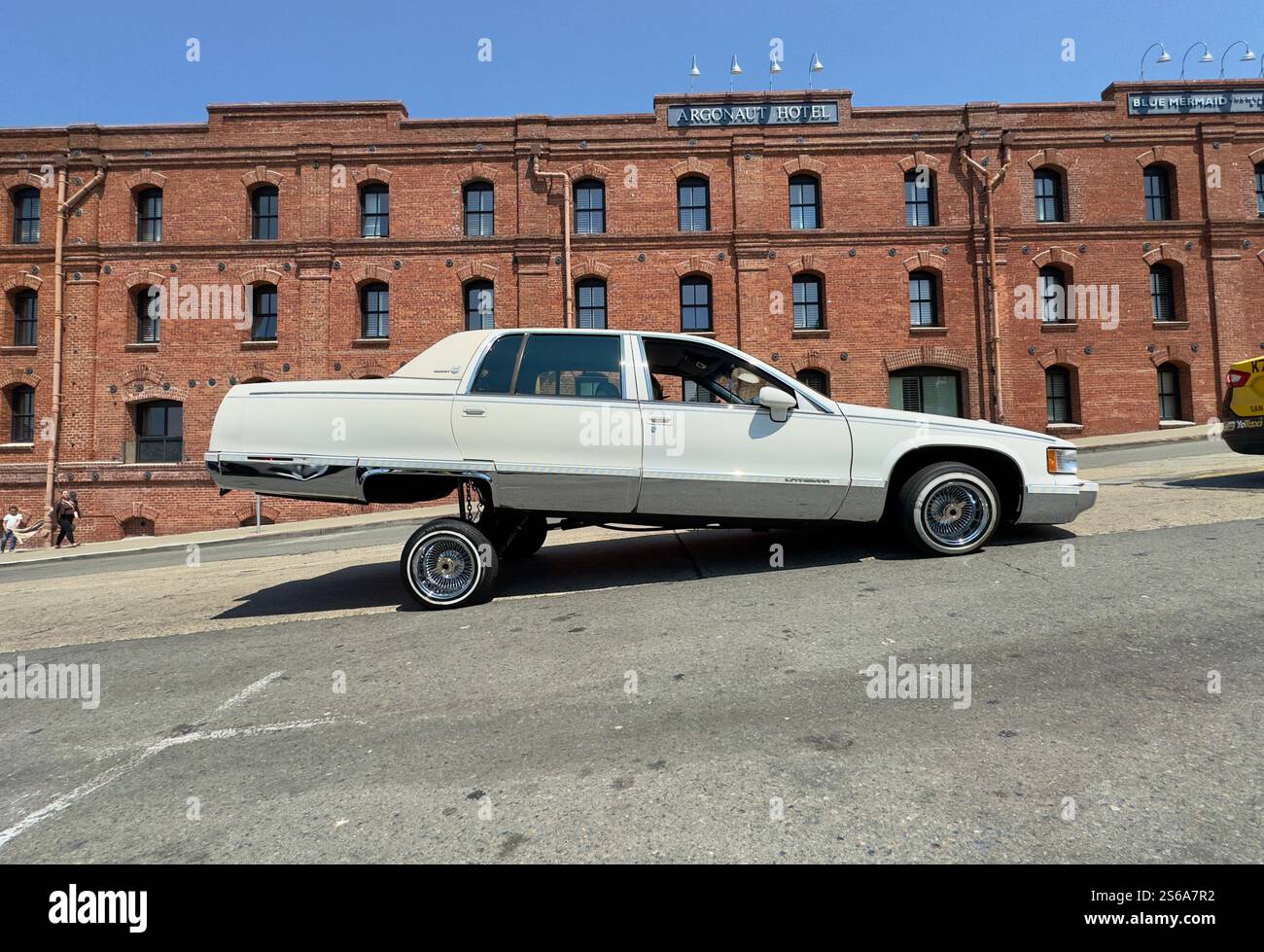 A classic white lowrider car with hydraulics raised on one side, parked ...