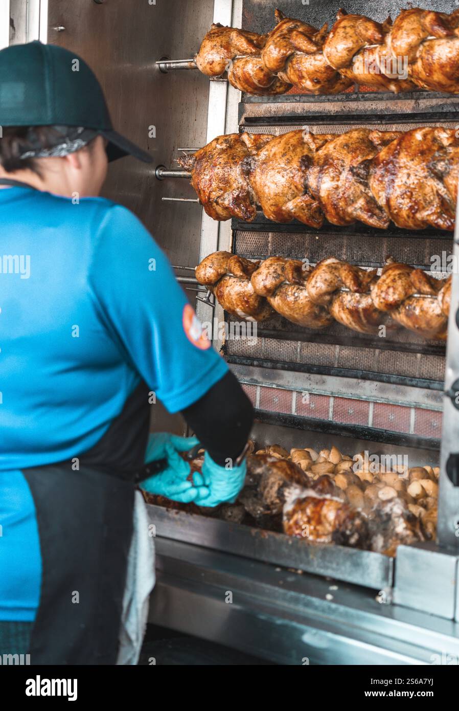 A worker preparing freshly roasted chickens on a rotisserie grill ...