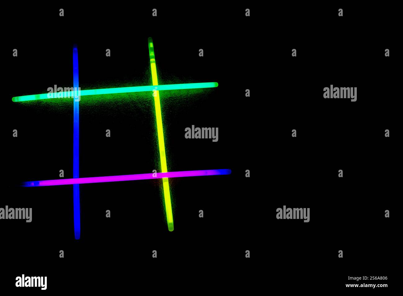 Neon glow sticks arranged in hashtag symbol on a black background ...