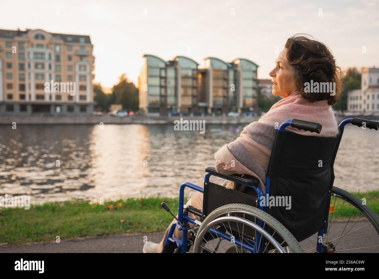 Sad senior woman sitting in wheelchair walking on road in city outdoor ...