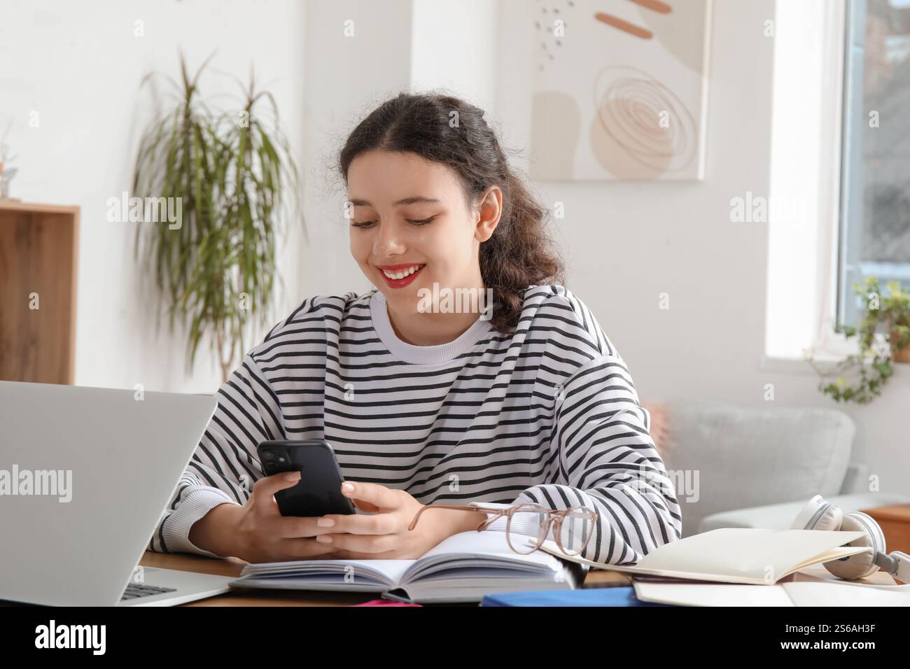 Female student using mobile phone while doing lessons at home Stock ...