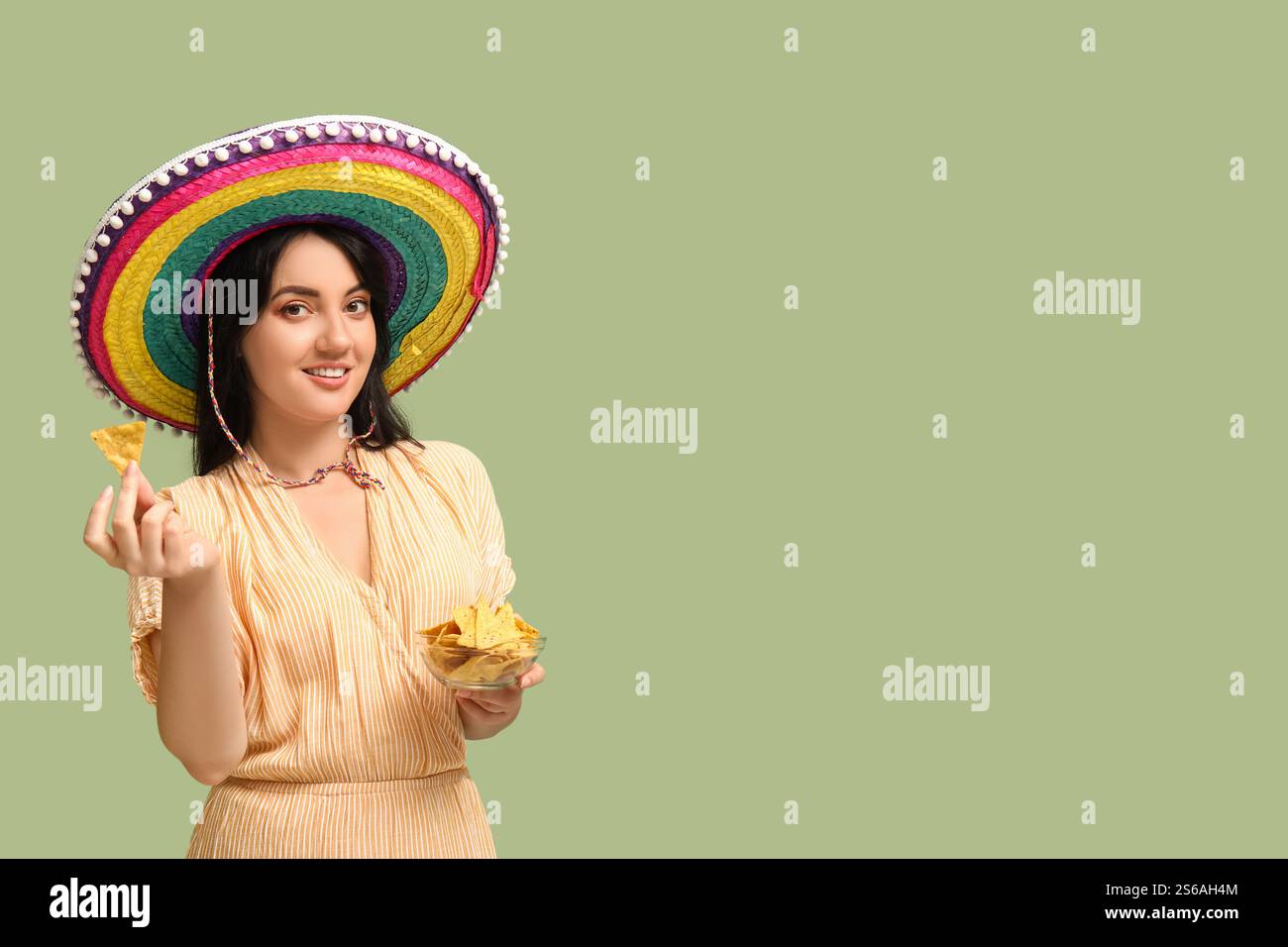 Beautiful Mexican woman in sombrero and with nachos on green background ...