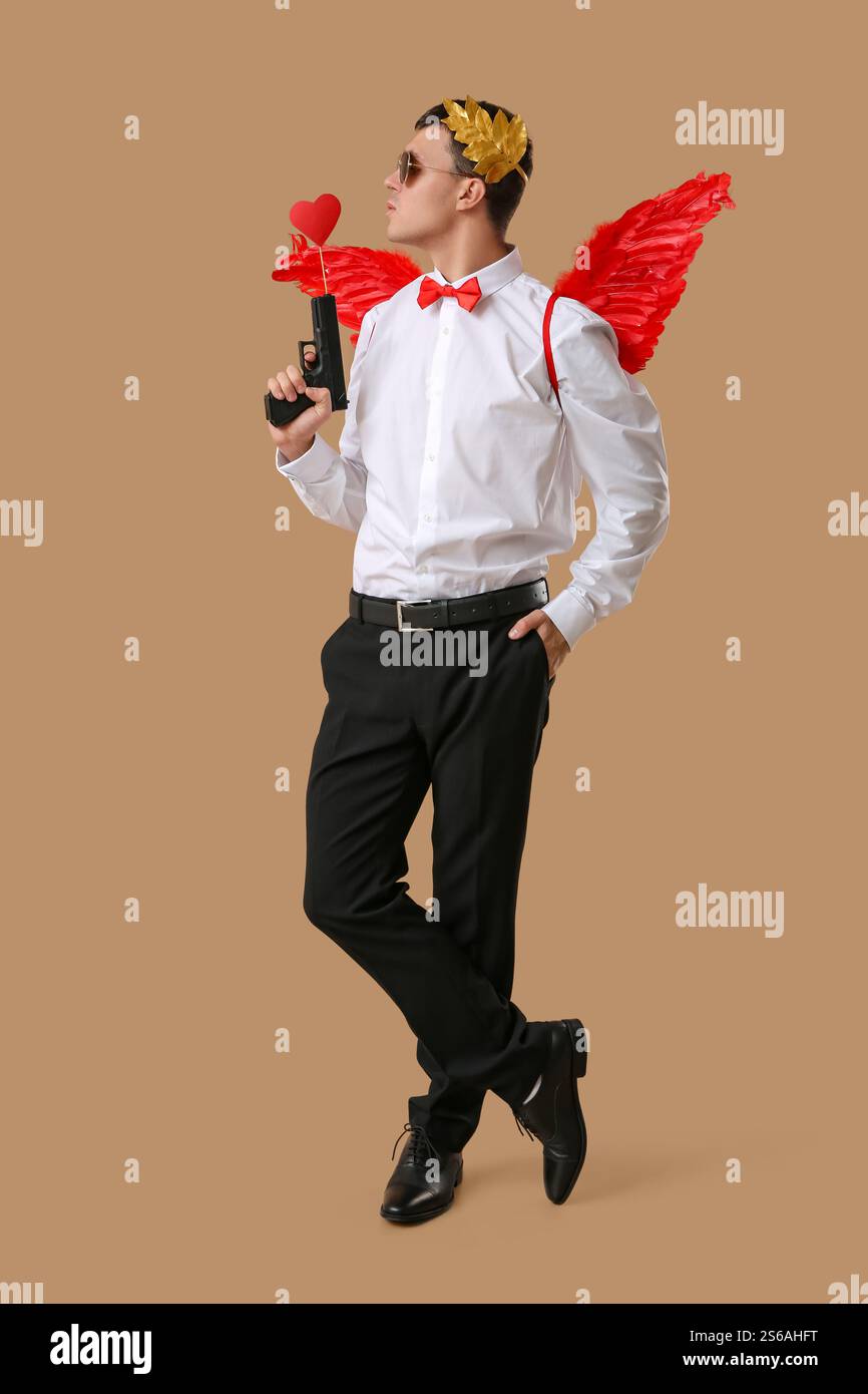 Cool young man dressed as Cupid with gun on beige background. Valentine ...