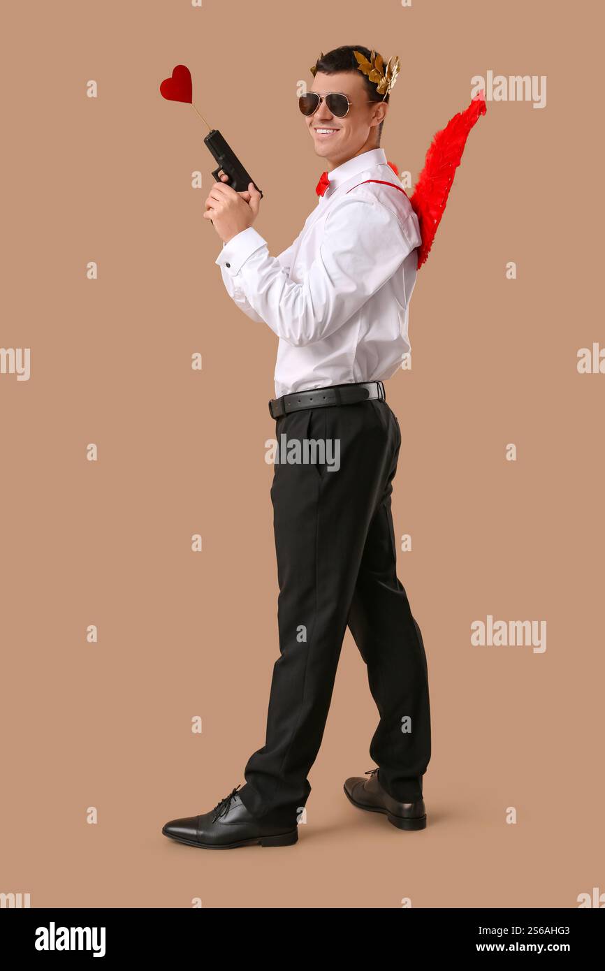 Cool young man dressed as Cupid with gun on beige background. Valentine ...