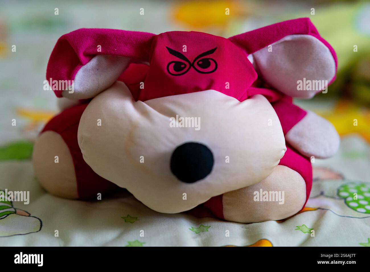 A fluffy red plush toy shaped like a dog sits on a vibrant bedspread ...