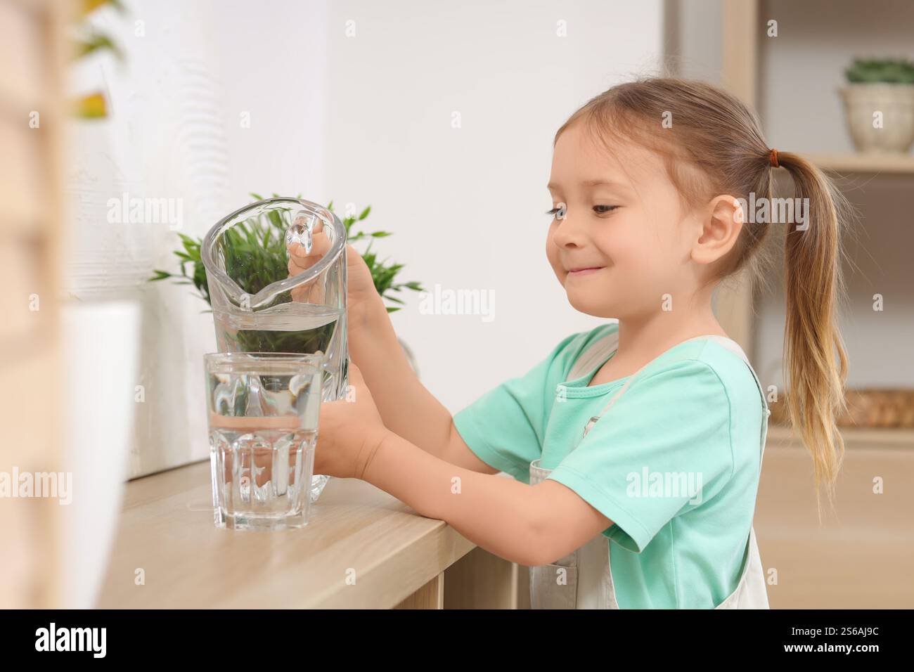 Cute little girl pouring water into glass on shelf at home Stock Photo - Alamy