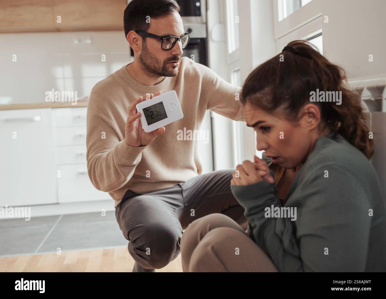 Young woman sitting beside radiator covered with sweater while man ...