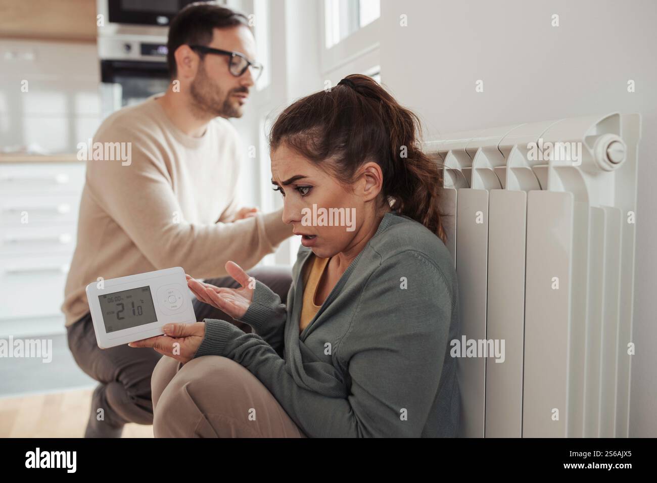 Young woman sitting beside radiator covered with sweater while man ...