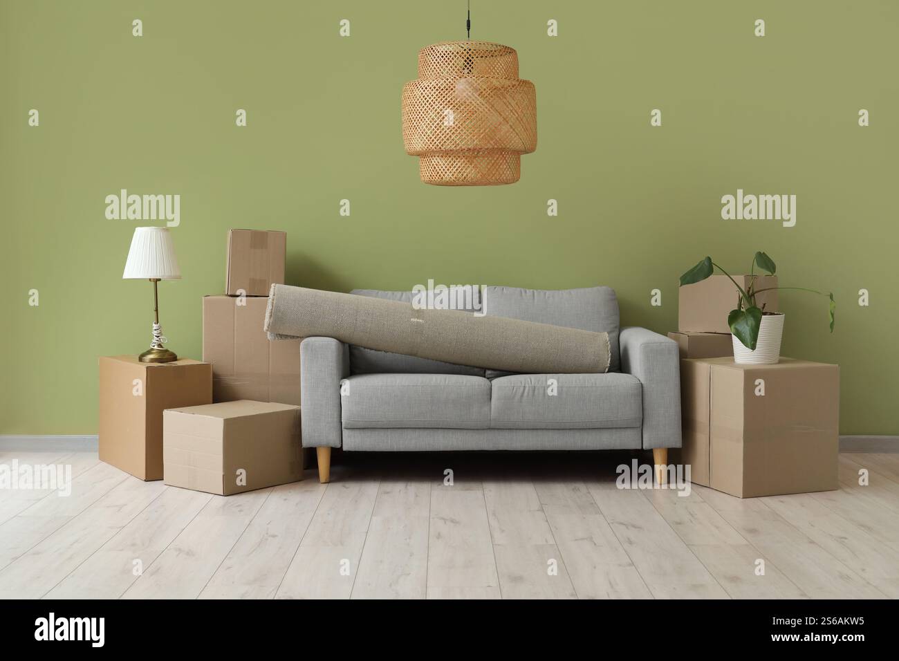Cardboard boxes with grey sofa, rolled carpet and lamp near green wall ...